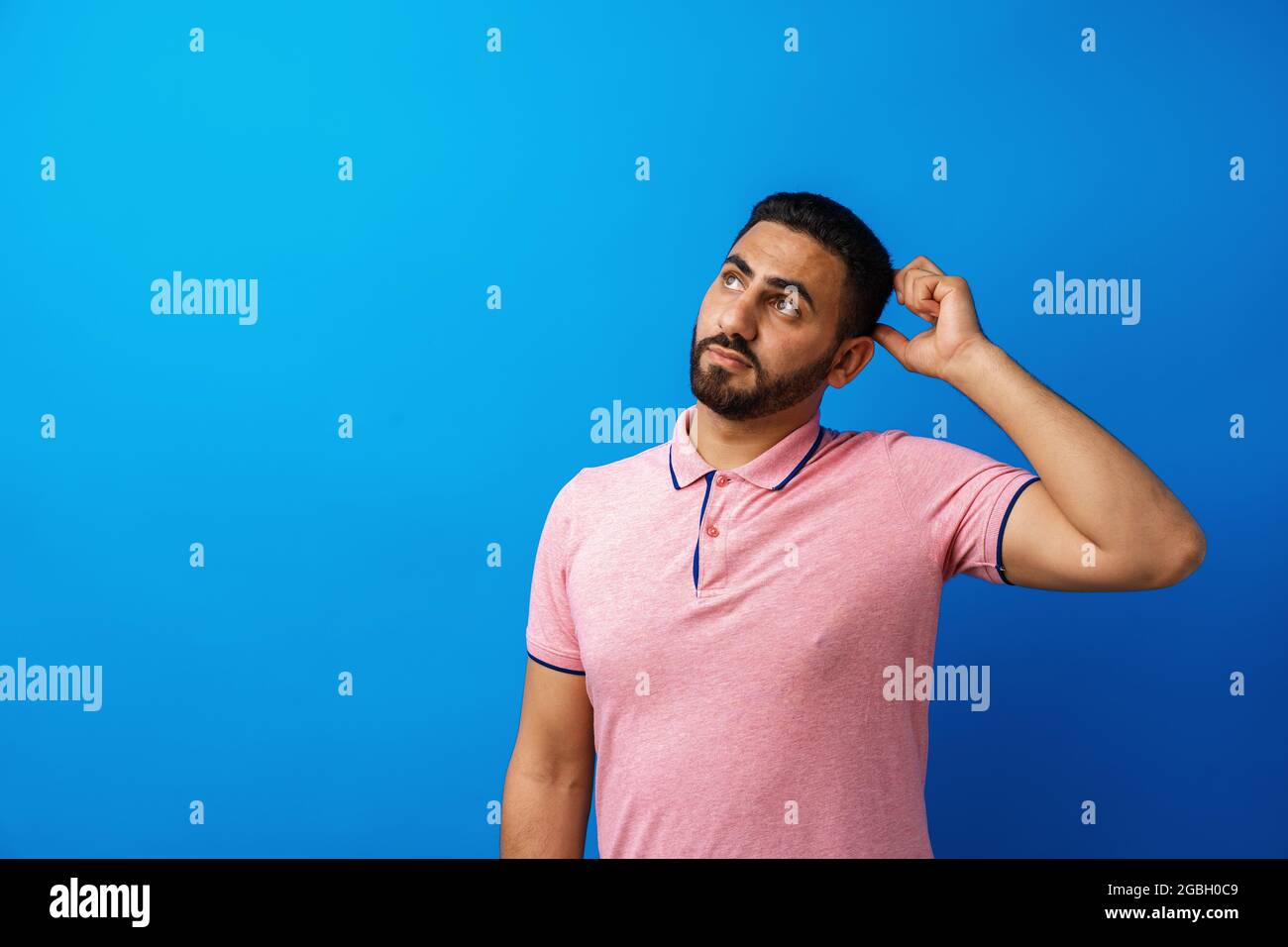 Pensive young arab man thinking and looking up against blue background ...