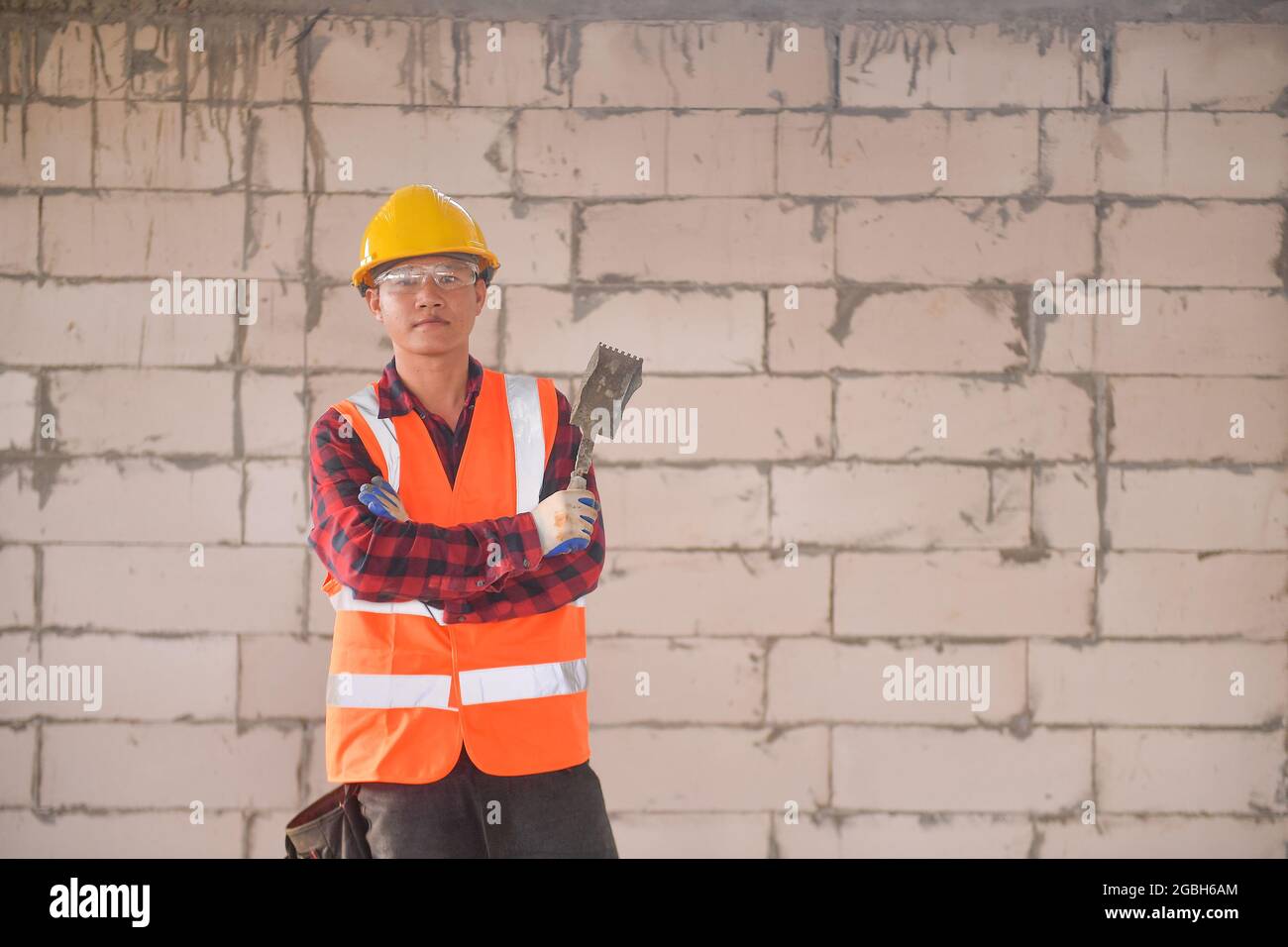 Portrait of a bricklayer standing on a building site in front of a wall ...