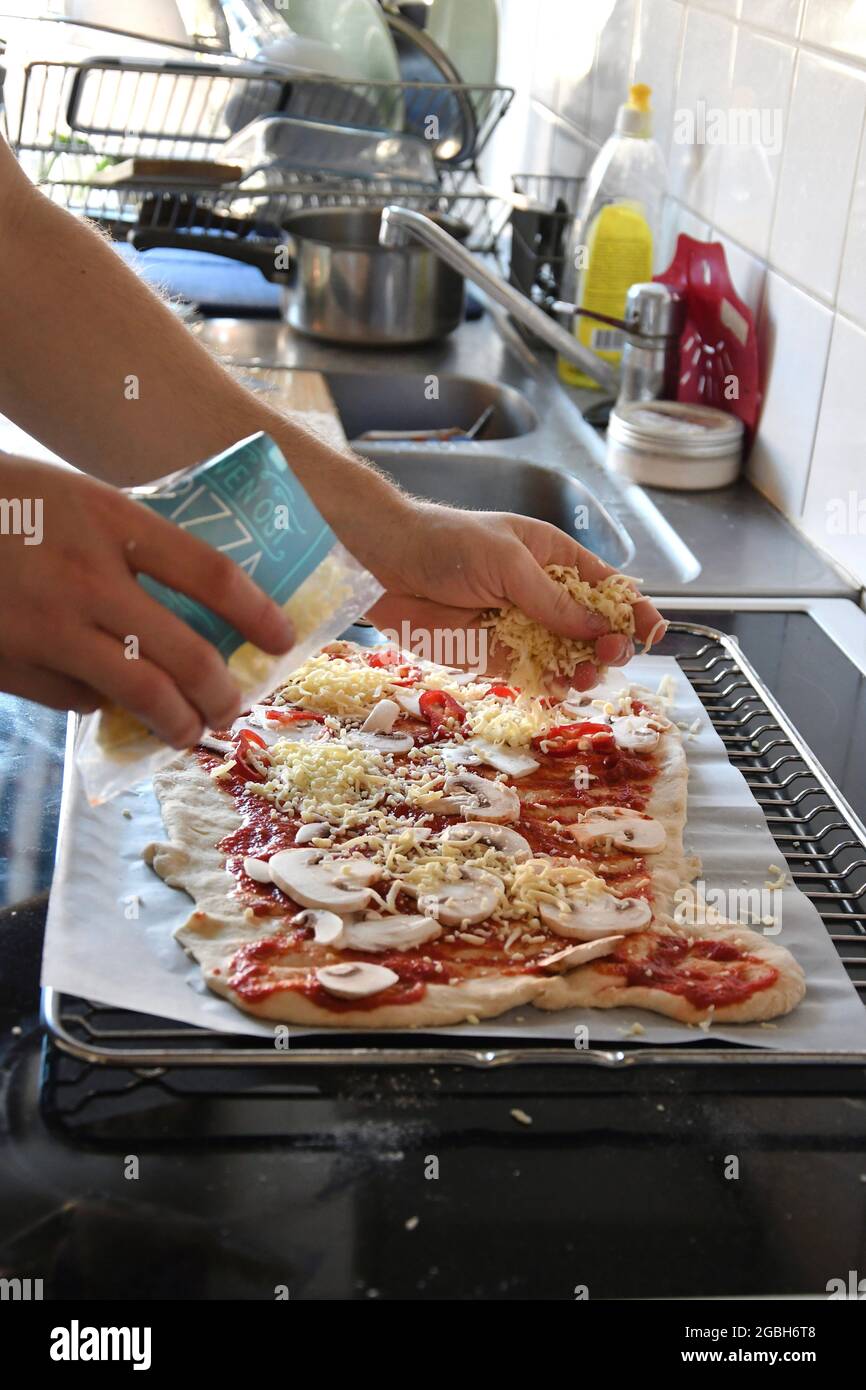 A man putting cheese on pizza, cooking food in the kitchen Stock Photo ...