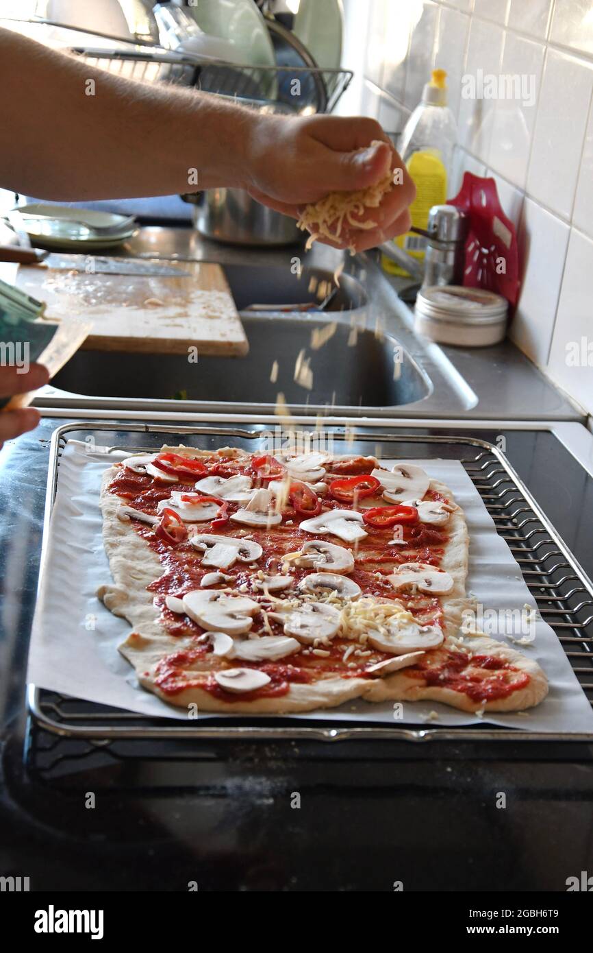 A man putting cheese on pizza, cooking food in the kitchen Stock Photo ...