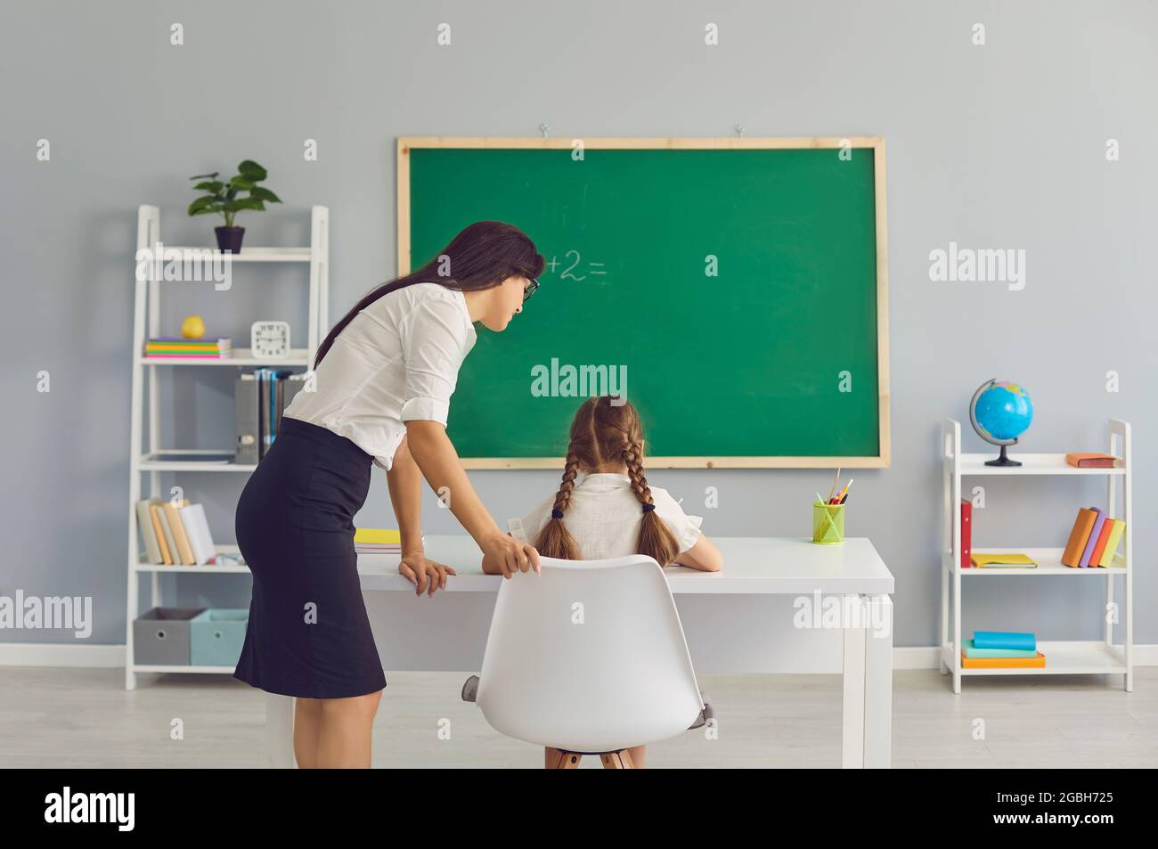 Female teacher helping little girl on math lesson at classroom. Tutor ...