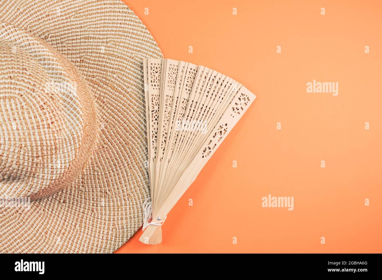 Round straw hat and a folding hand fan isolated on a peach background ...