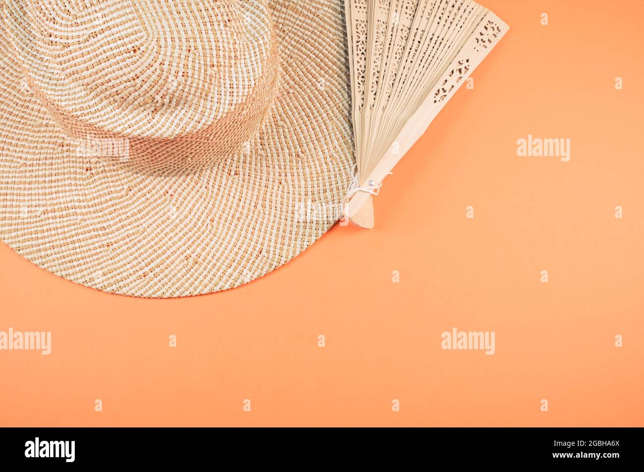 Round straw hat and a folding hand fan isolated on a peach background ...