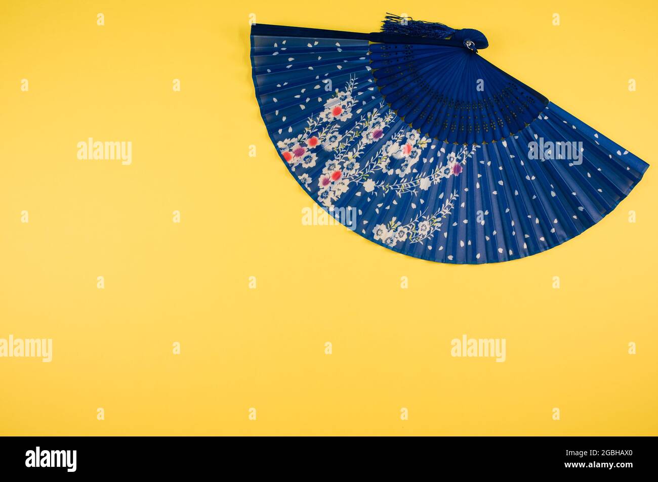 Blue folding hand fan isolated on a yellow background with free space ...