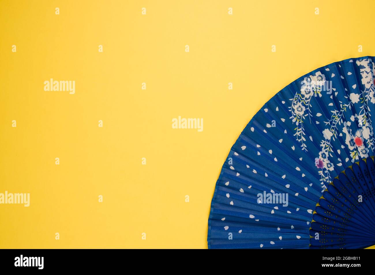 Blue folding hand fan isolated on a yellow background with free space ...