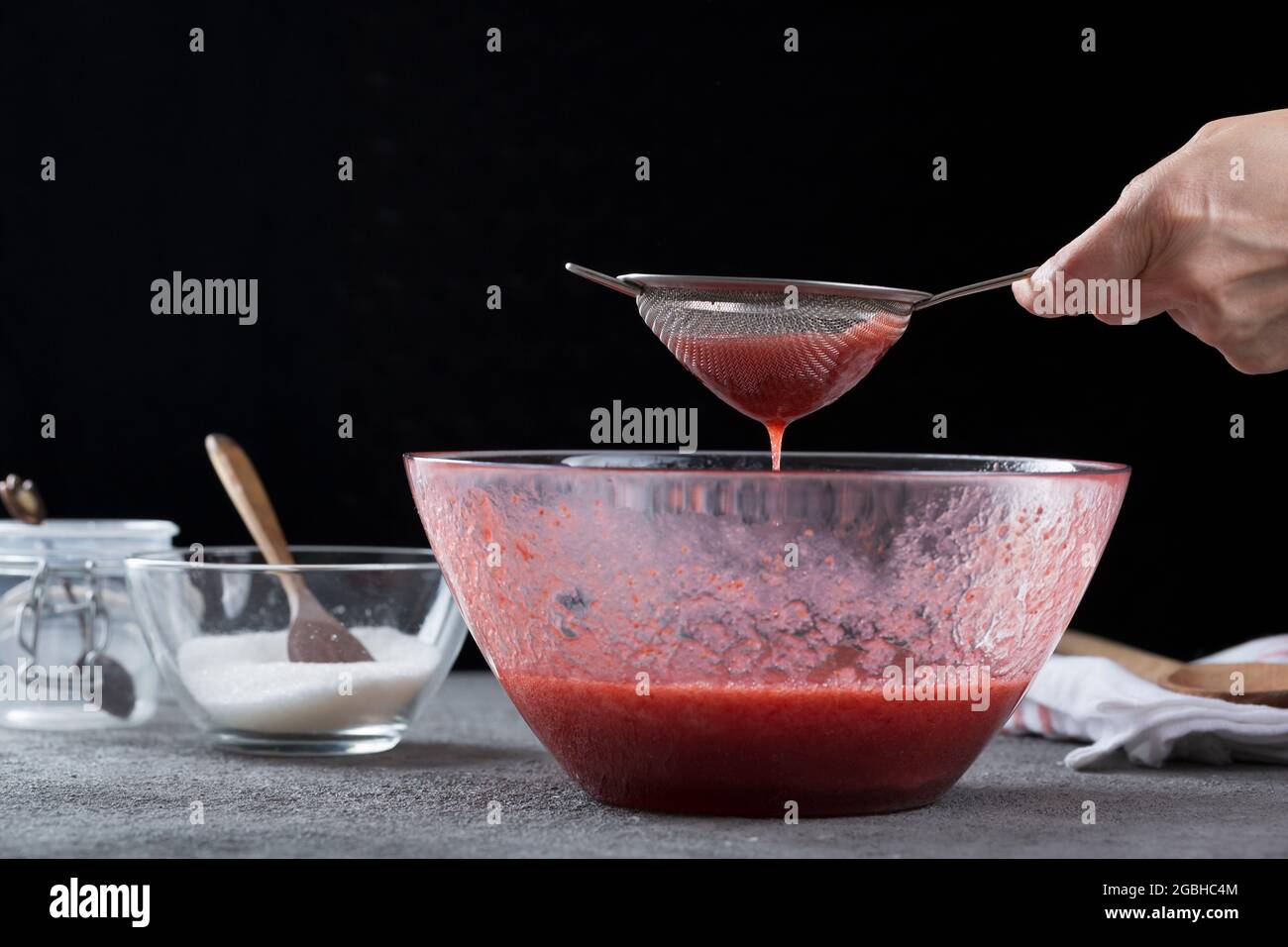 Woman straining strawberry jam through a sieve, home cooking and ...