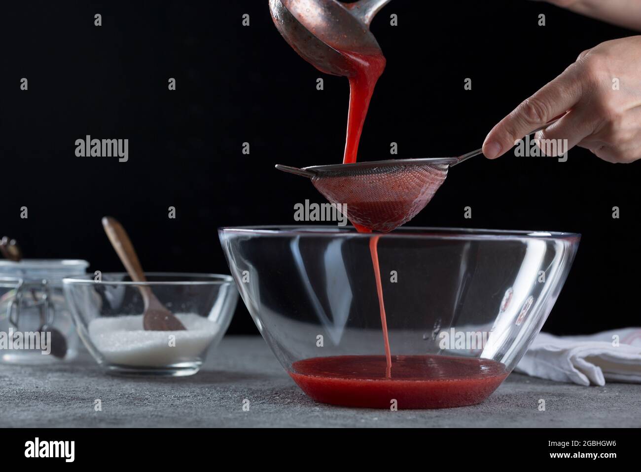 Woman straining strawberry jam through a sieve, home cooking and ...