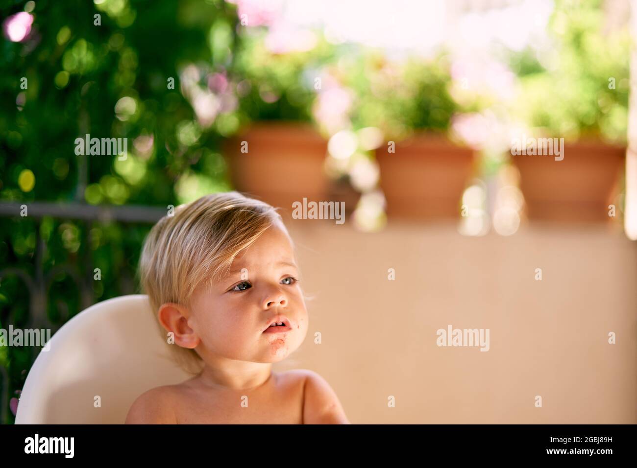 Serious child with a stained chin sits on a high chair on the balcony ...