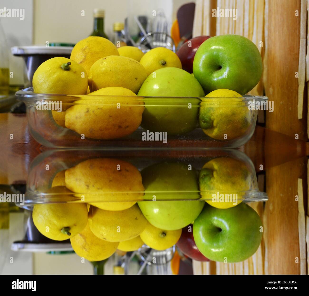 Fresh apples and lemons on a glass container with reflection on a table ...