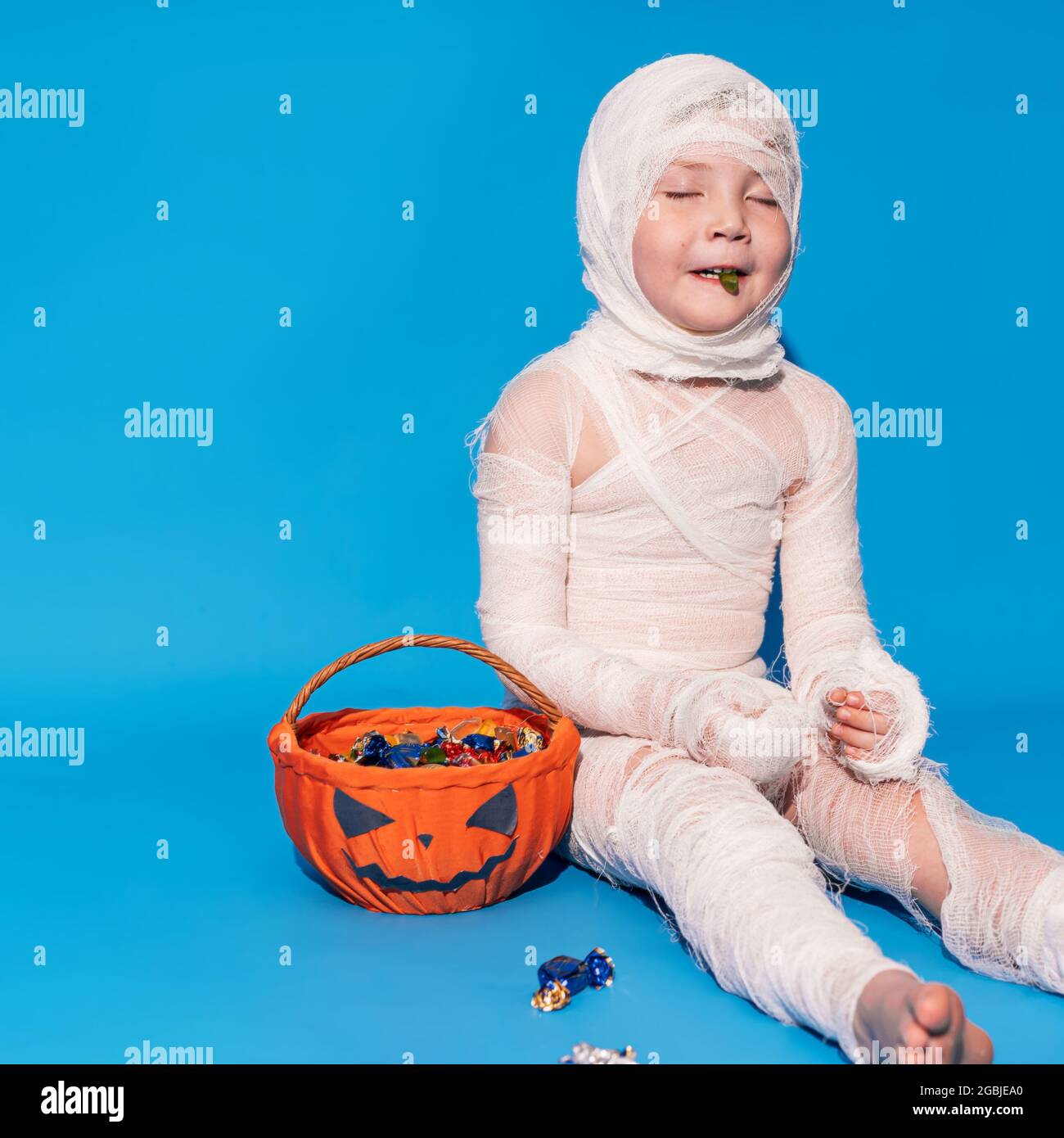 Child in mummy costume eats candies from basket in the form of pumpkin ...