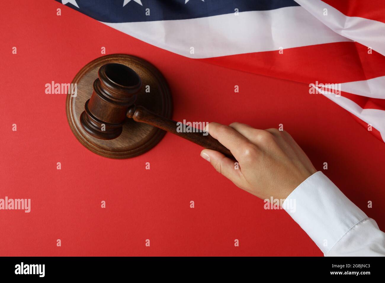 Female hand judge holds gavel on red background with american flag ...