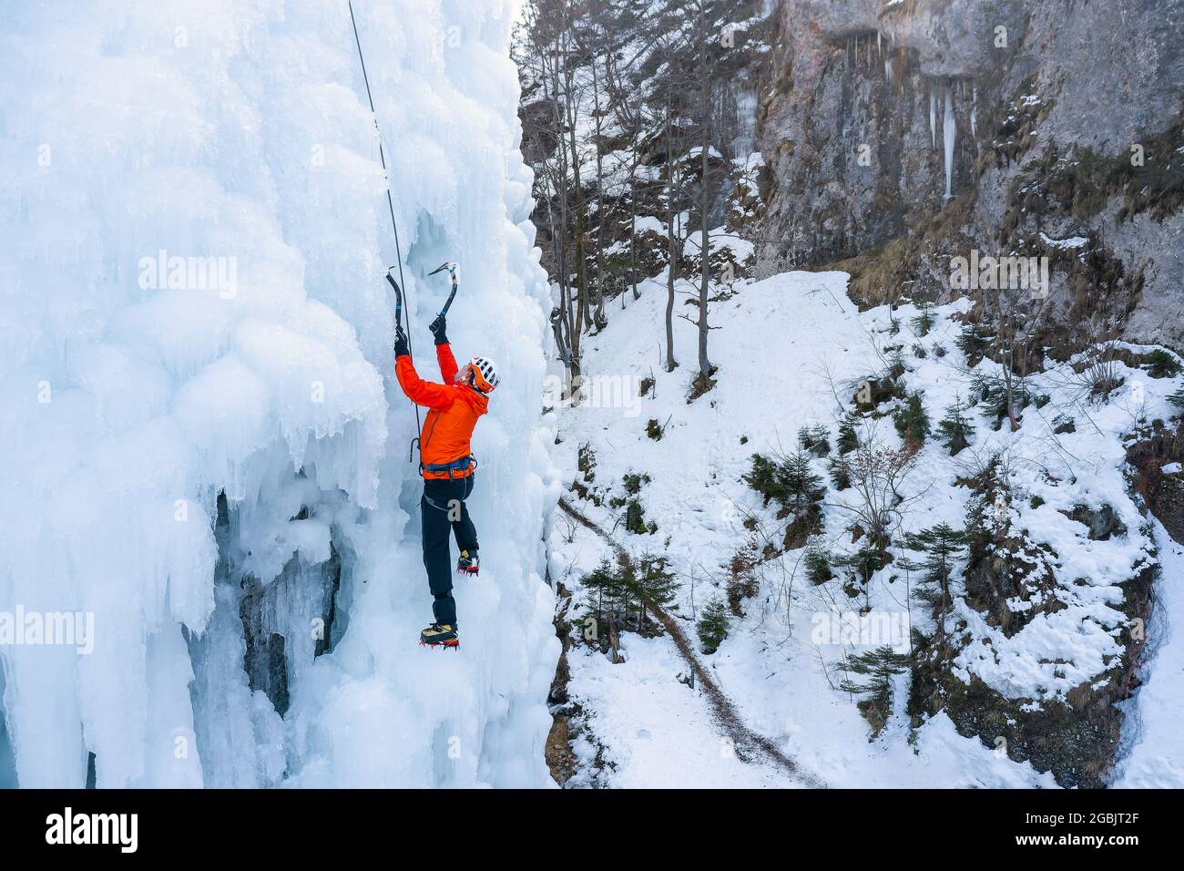Male athlete doing a vertical ice climb, kicking front crampons into ...