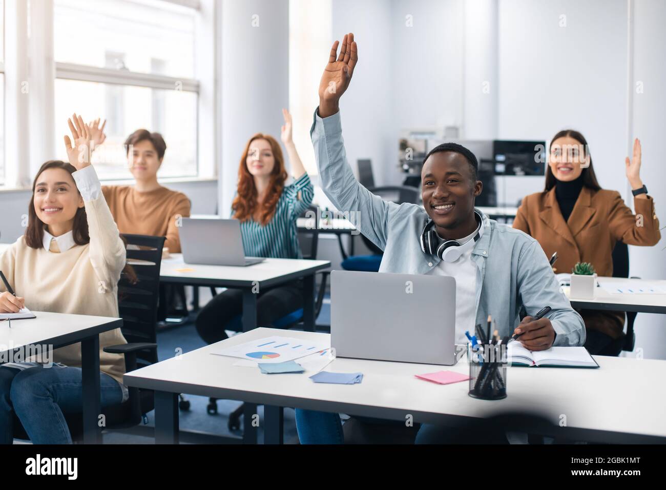Portrait of diverse students raising hands at modern classroom Stock ...