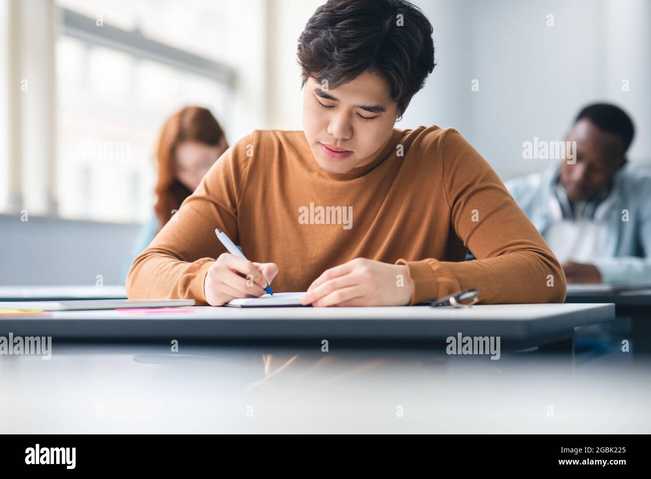 Asian male student sitting at desk in classroom writing exam Stock ...
