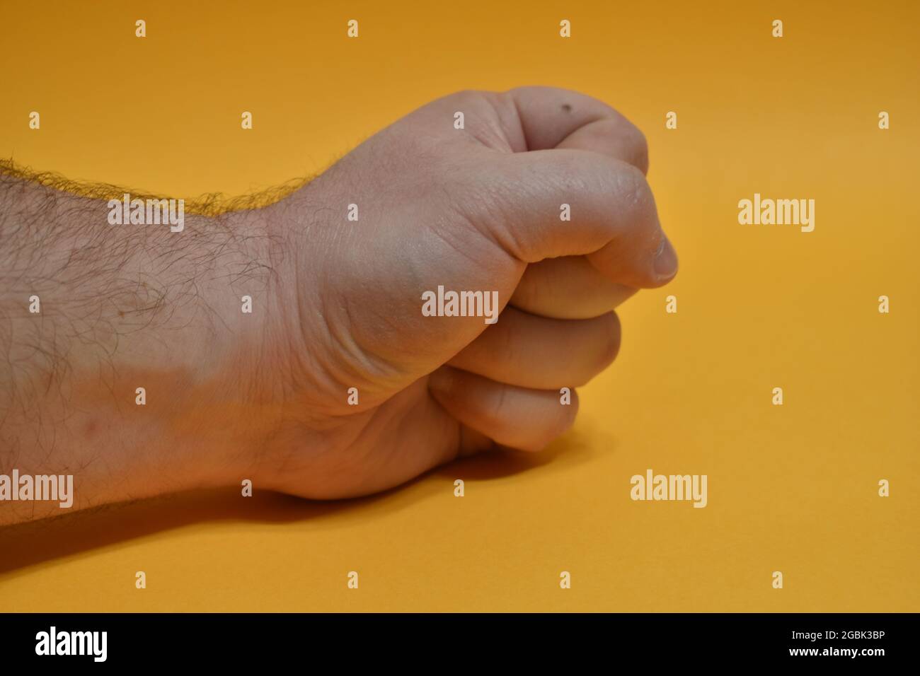 Male's pounding fist on a yellow background Stock Photo - Alamy