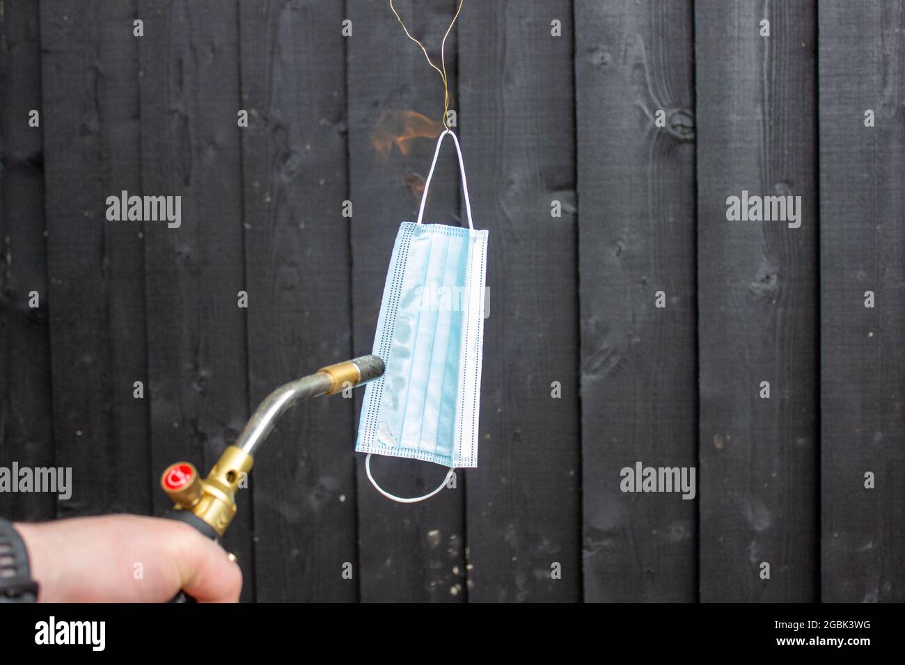 Man trying to burn a single-use mask on a wooden wall background ...