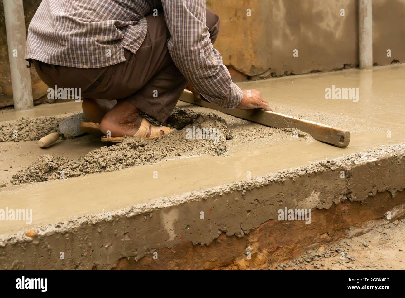 Indian construction worker levelling a cemented floor using wooden ...