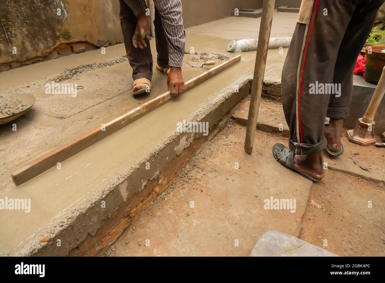 Indian construction worker levelling a cemented floor using wooden tool ...
