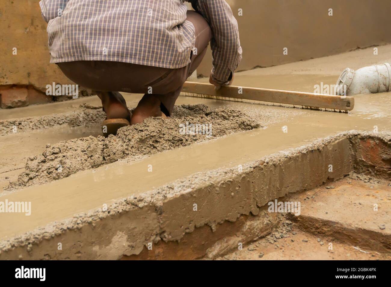 Indian construction worker levelling a cemented floor using wooden ...