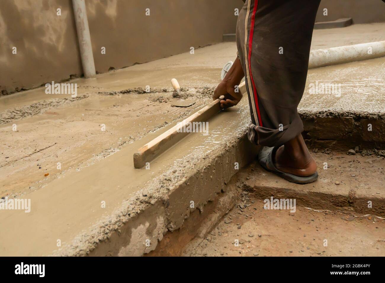 Indian construction worker levelling a cemented floor using wooden tool ...