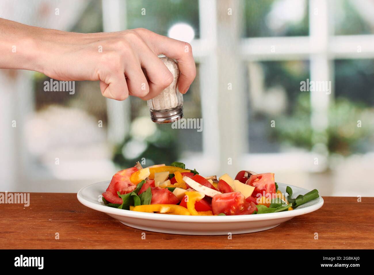 Hand adding salt using salt shaker on bright background Stock Photo - Alamy