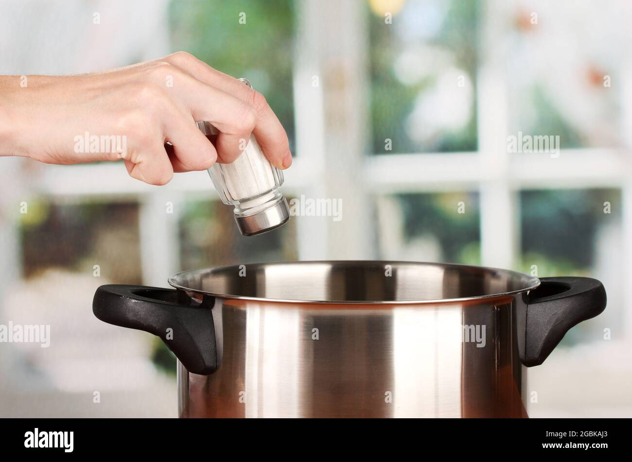 Hand adding salt using salt shaker on bright background Stock Photo - Alamy