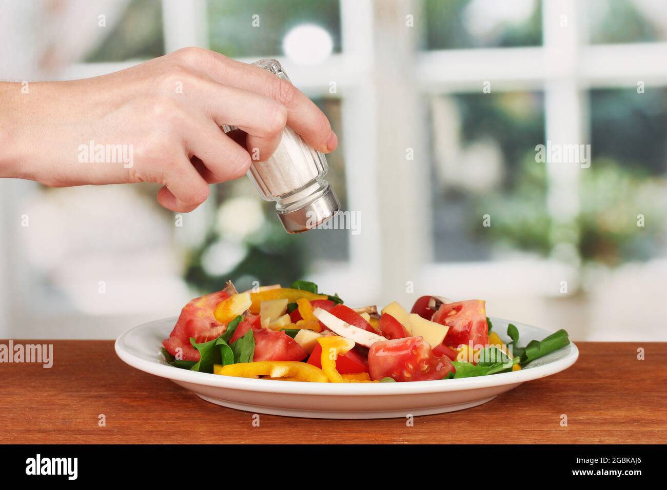 Hand adding salt using salt shaker on bright background Stock Photo - Alamy