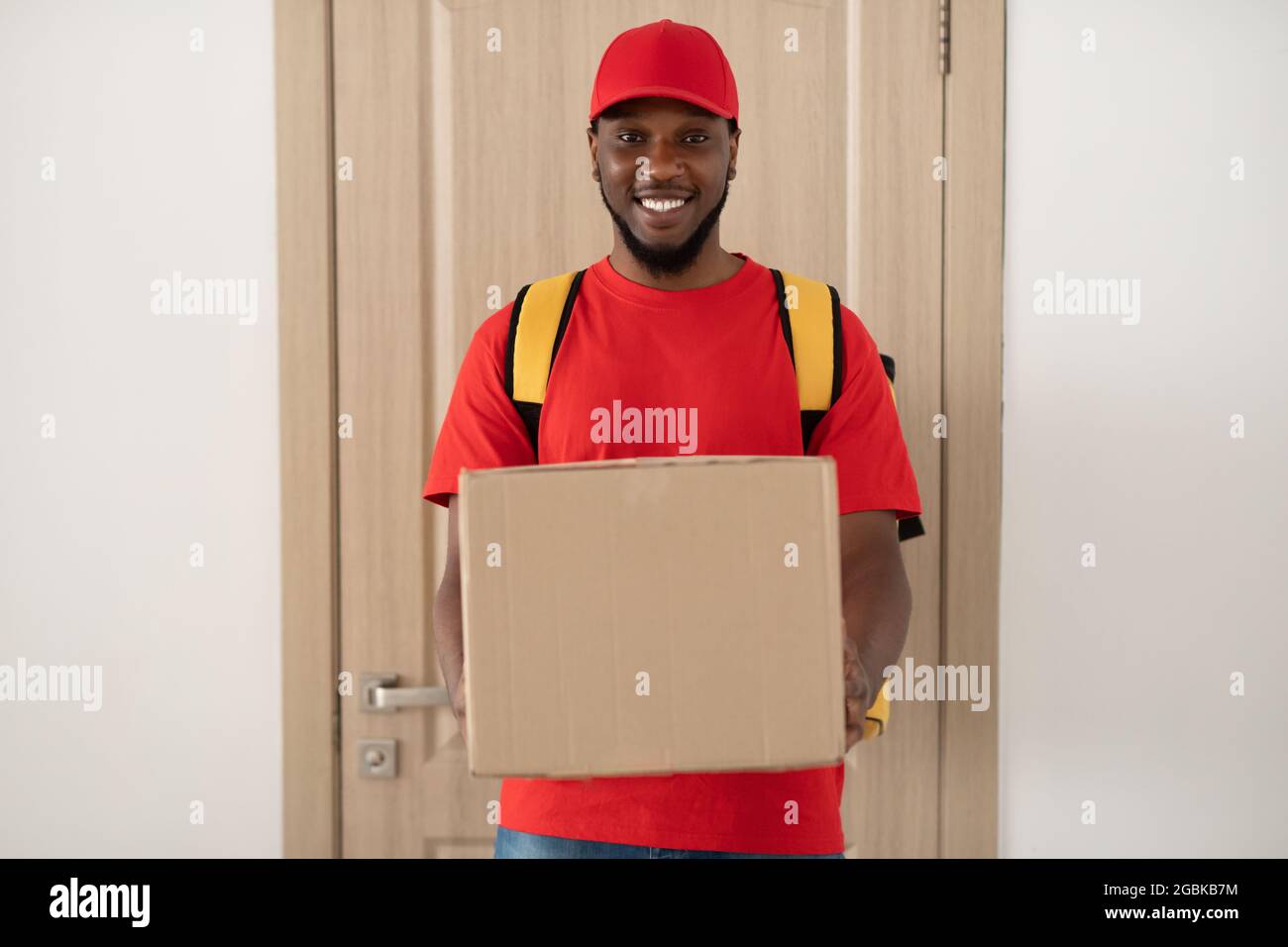 Black delivery man holding box standing at door Stock Photo - Alamy