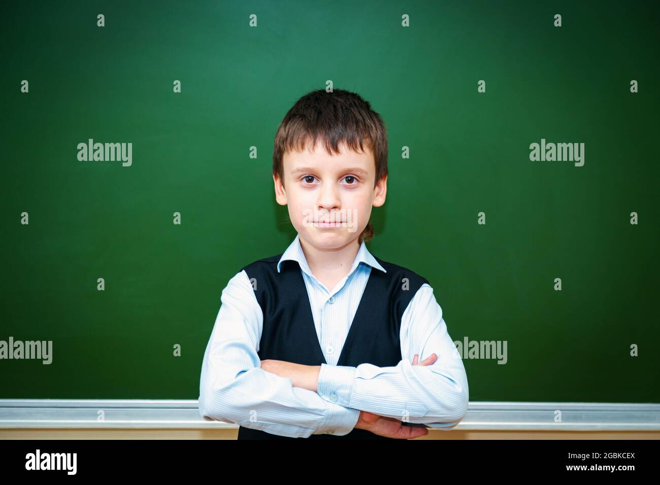 Serious schoolboy near the green school board in the classroom ...