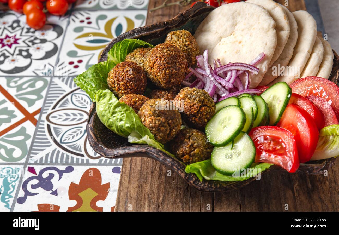 Falafel, fresh vegetables and pita bread on clay plate, gray background ...