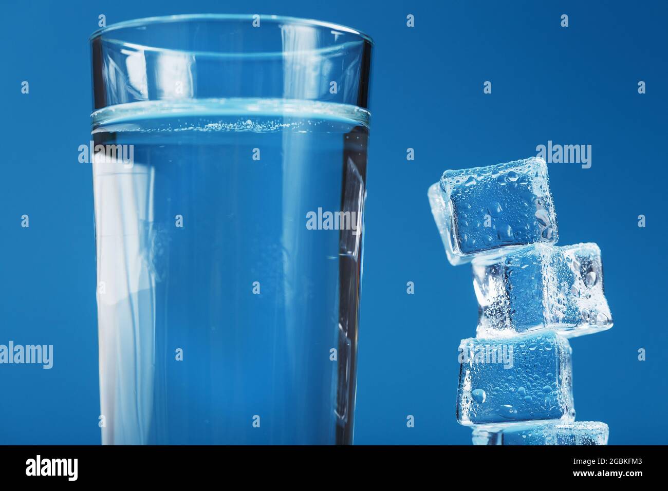 Ice cubes tower with a glass of cold and clean water on a blue ...