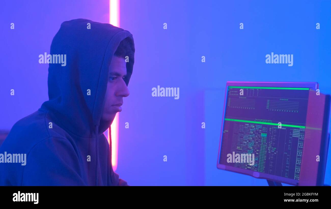 Profile view of african hacker in hoodie working in room filled with ...