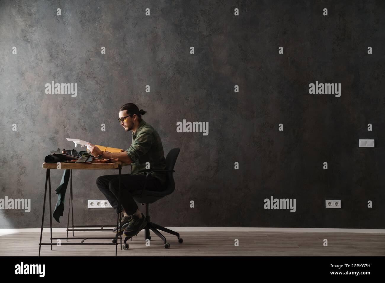 Bearded focused craftsman writing down notes while working with leather ...