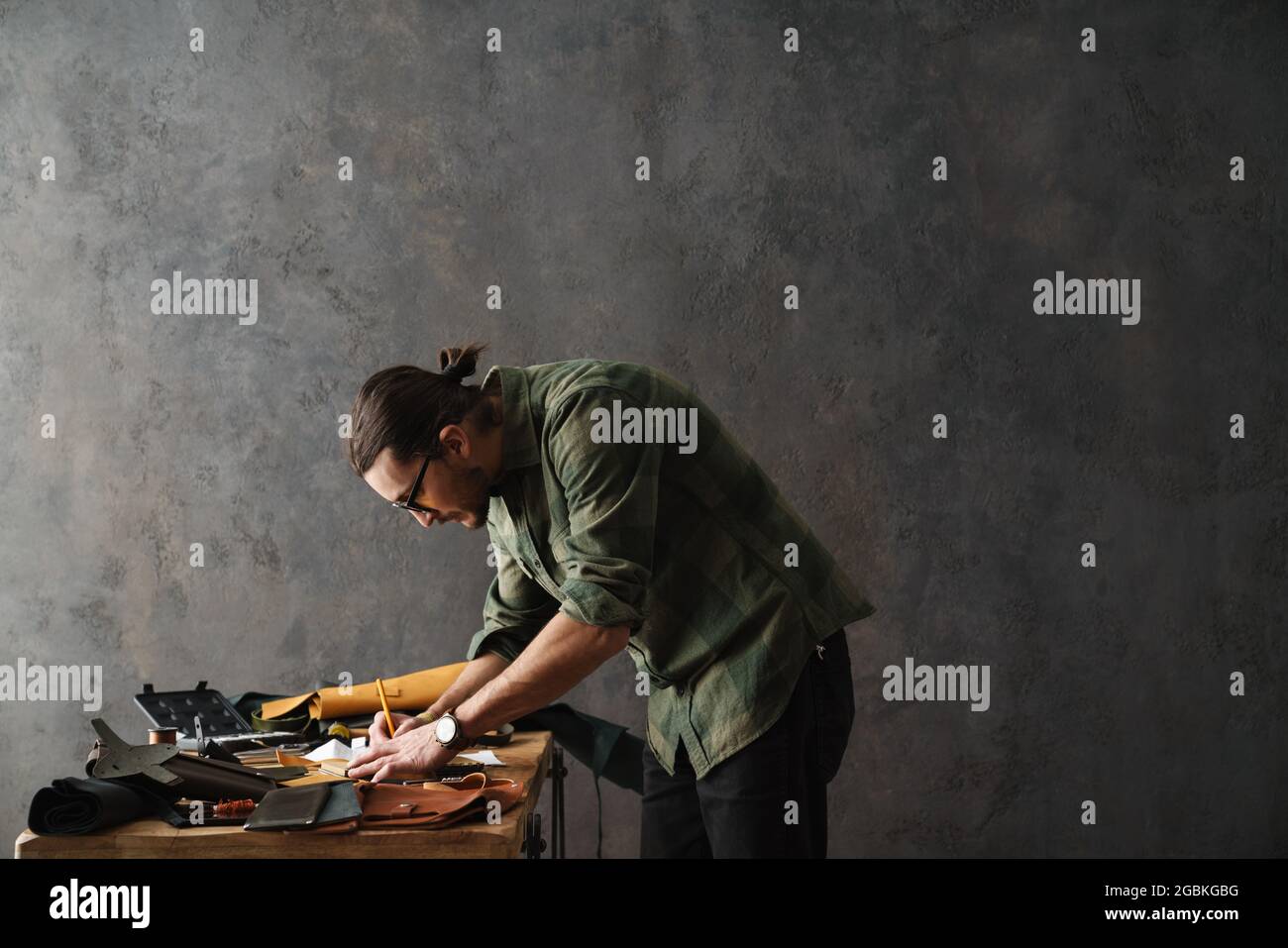 Bearded focused craftsman working with leather while standing at table ...