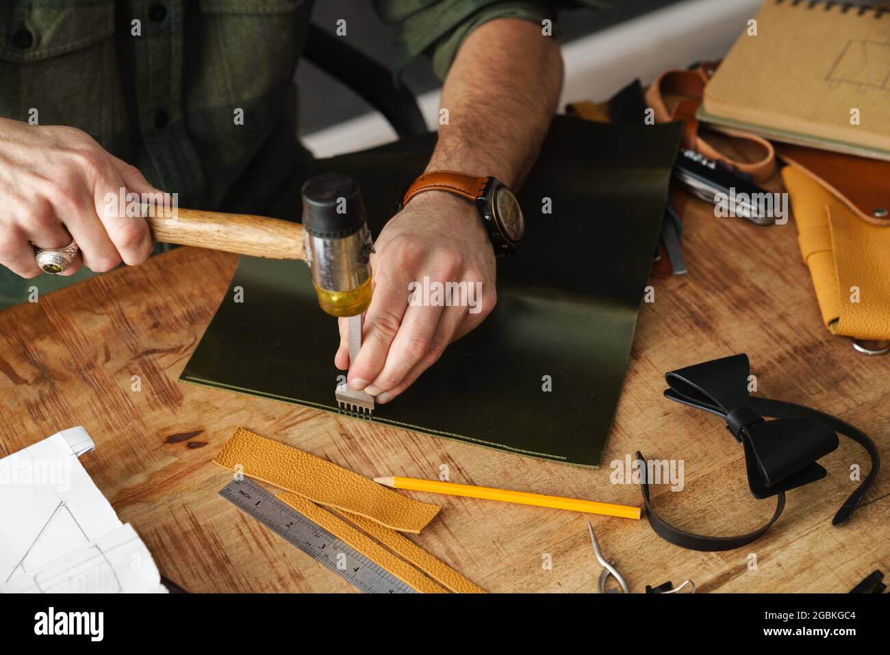 White craftsman using hummer while working with leather in workshop ...