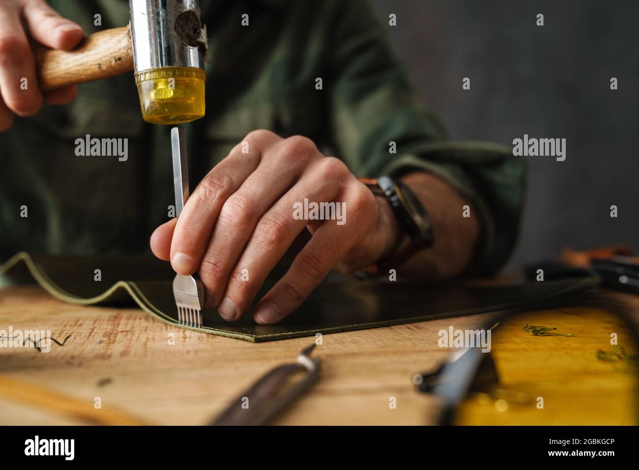 White craftsman using hummer while working with leather in workshop ...