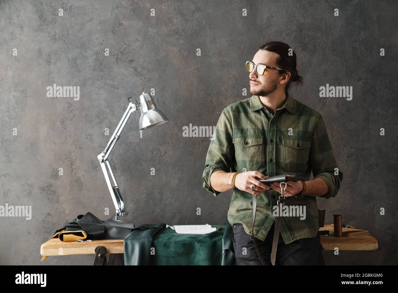 Bearded white craftsman standing with leather clutch in his workshop ...