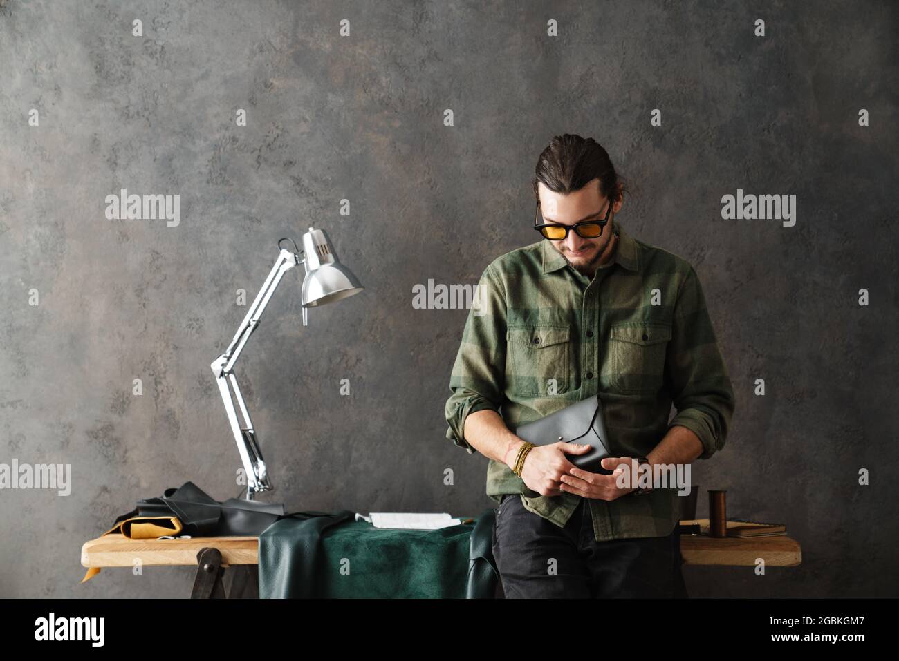 Bearded white craftsman standing with leather clutch in his workshop ...