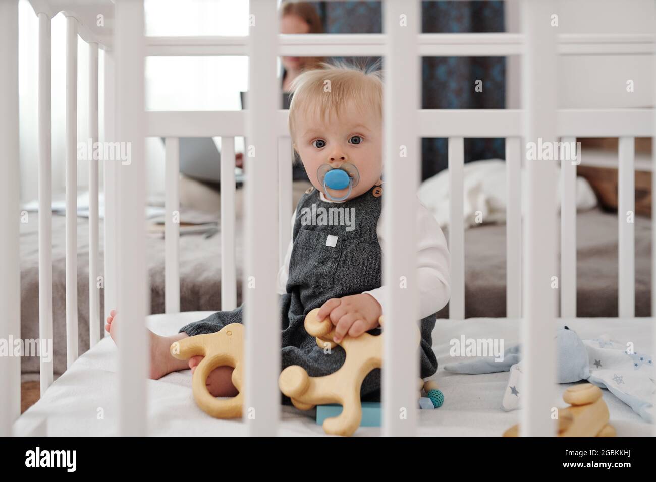 Portrait of serious cute baby in bodysuit sitting with wooden toy ...