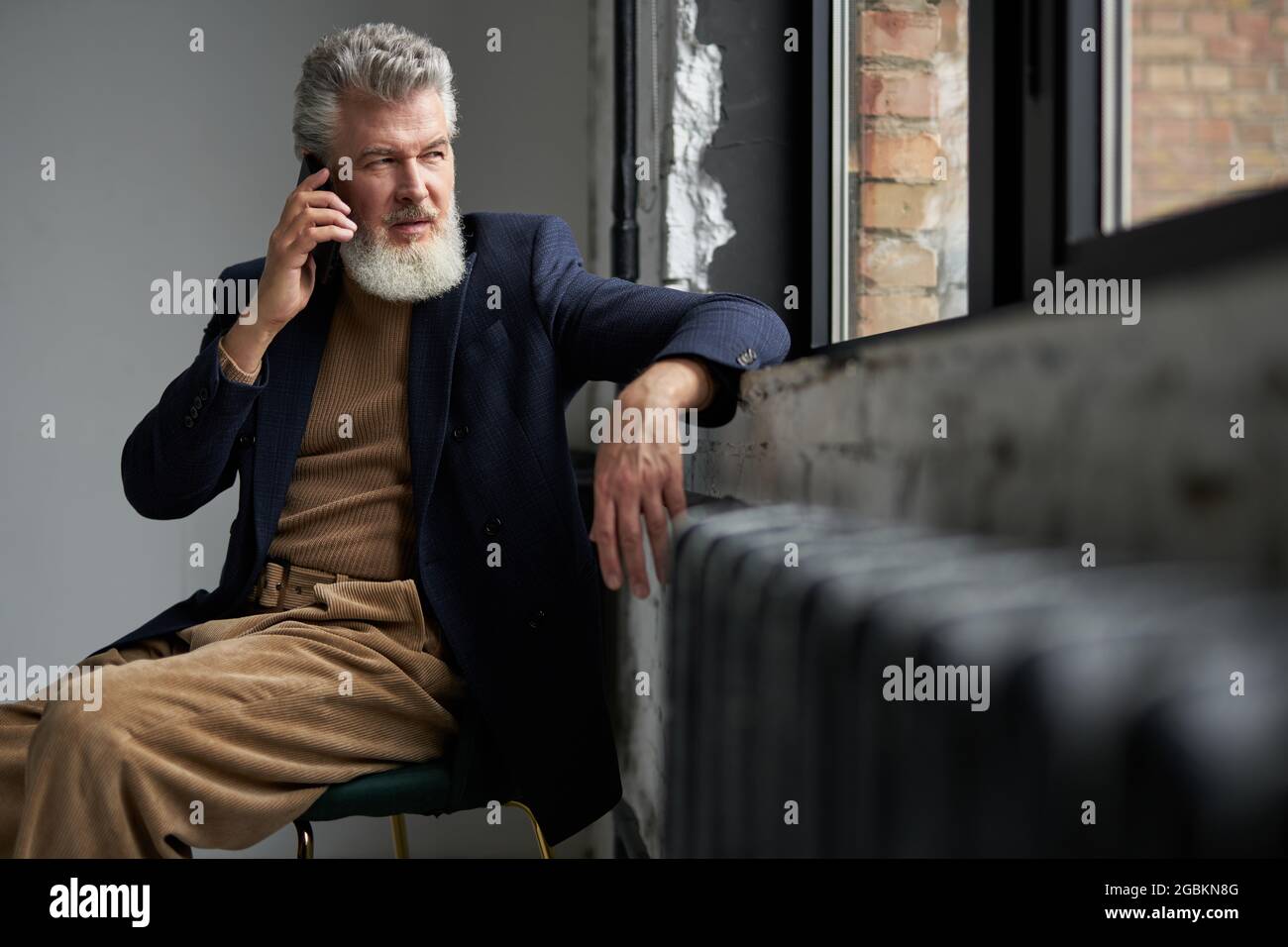 Stylish gray haired middle aged man in casual wear looking out a window ...