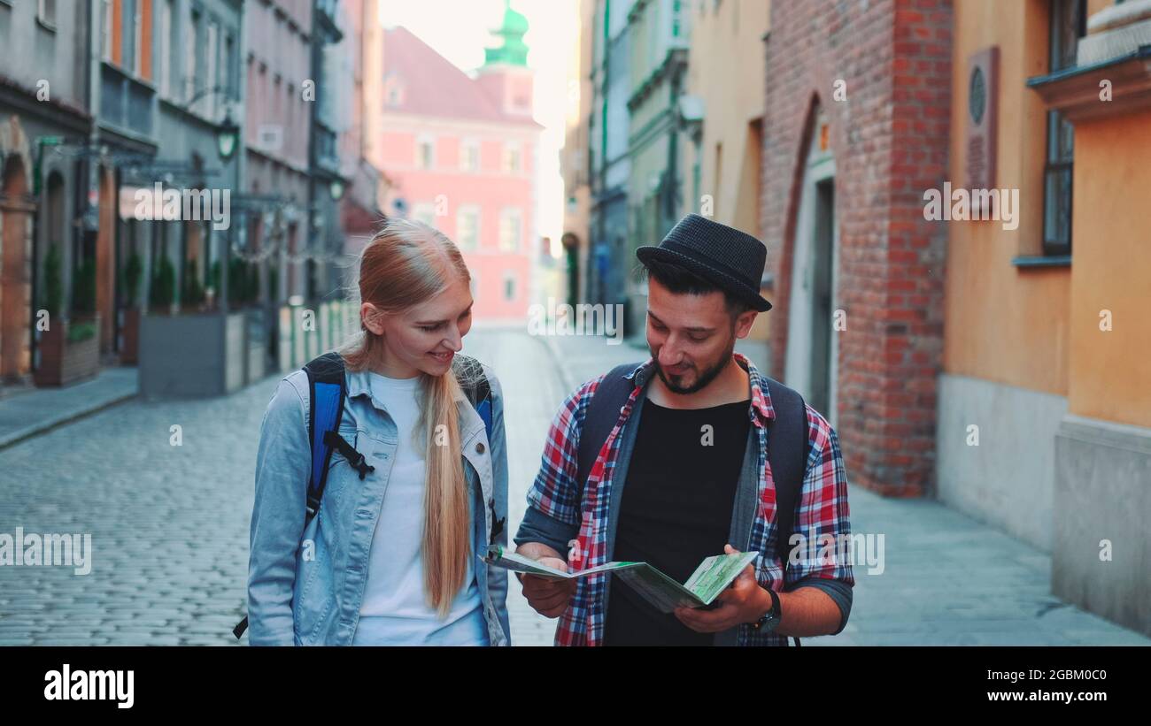 Two young tourists checking map while walking on main tourist street ...