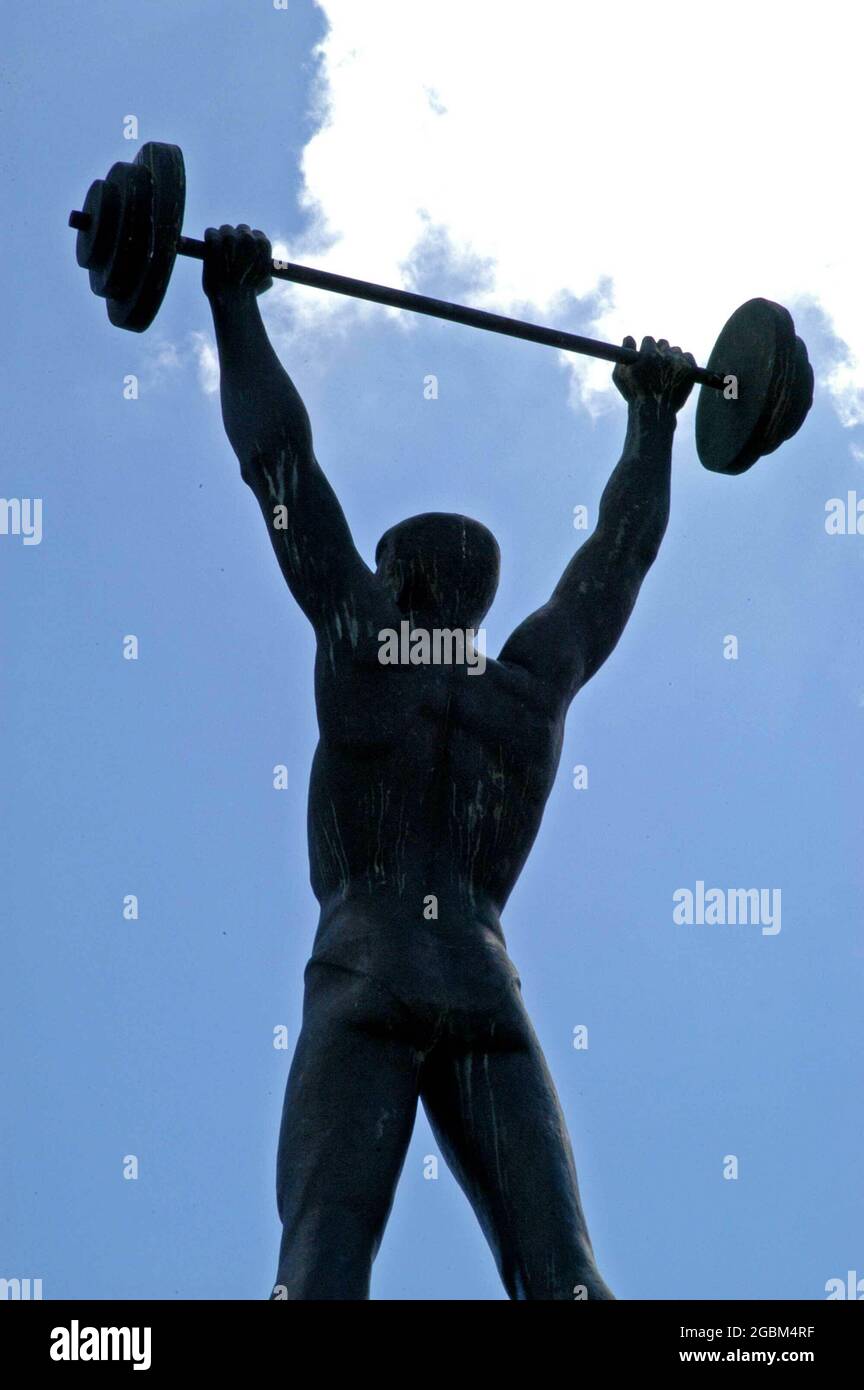 Vertical shot of a statue of a weightlifter lifting a barbell against a ...