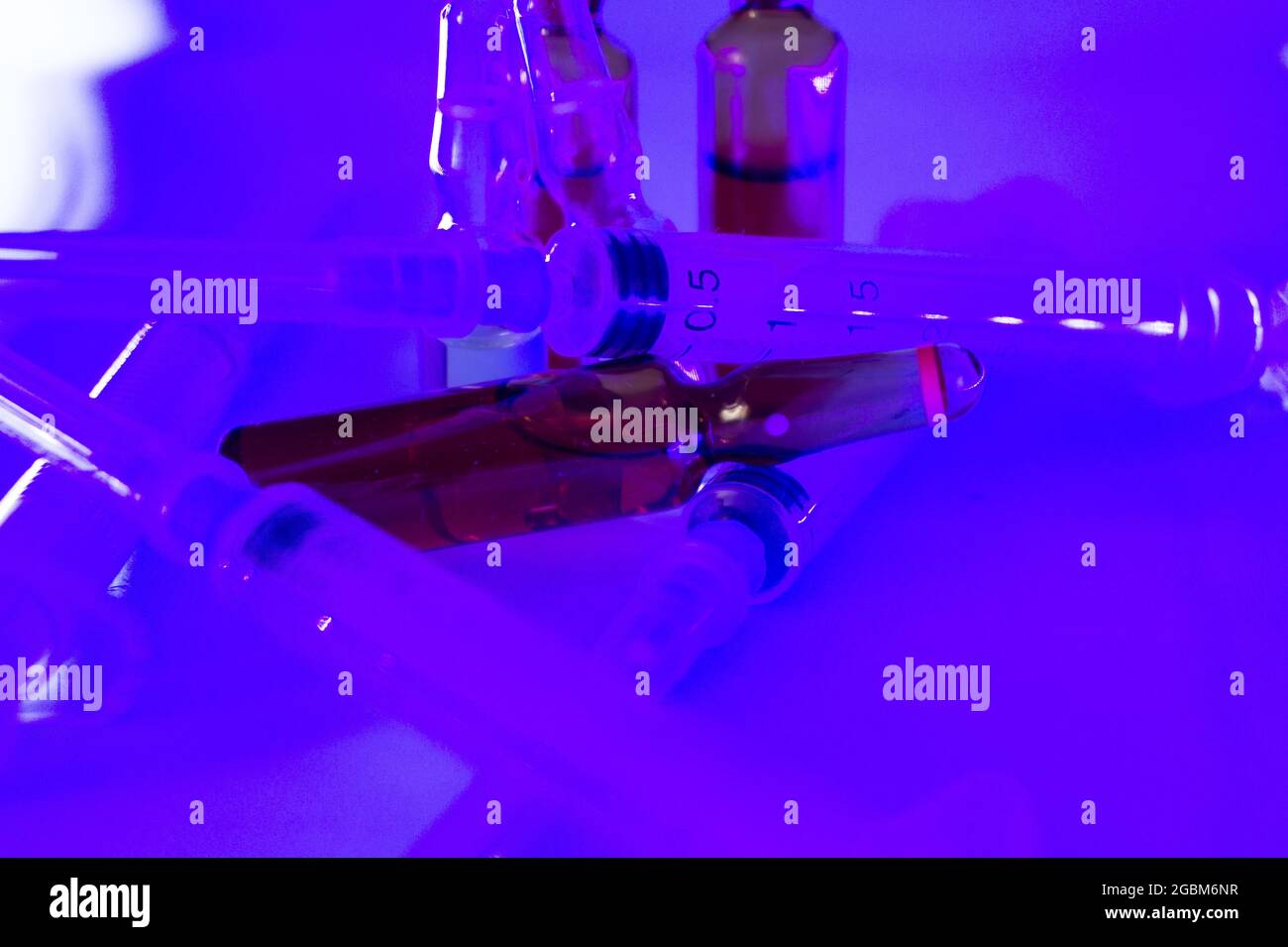 Syringes on a purple surface with reflections in it in a dark room ...