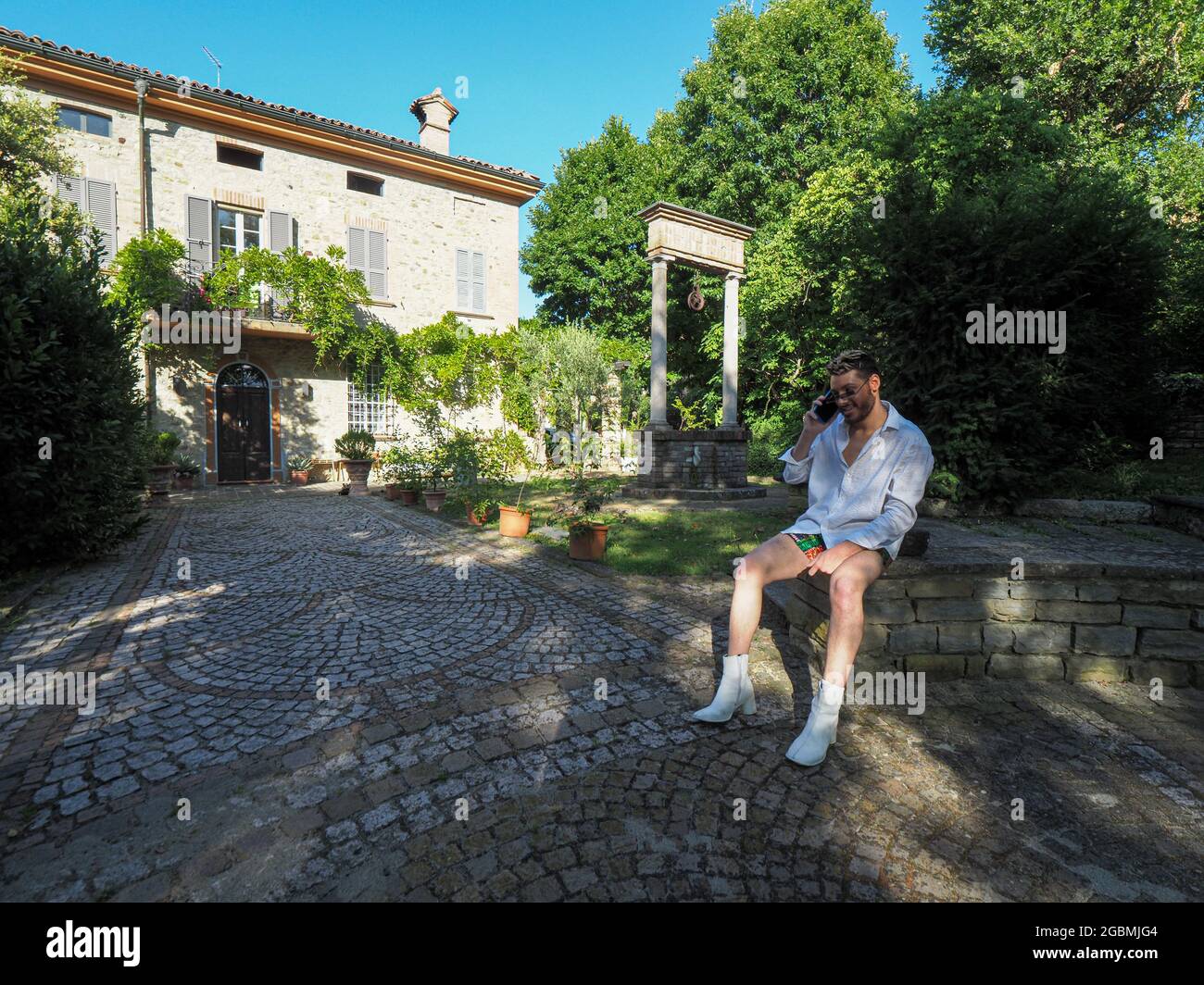 Gender-fluid Caucasian Italian person sitting in a garden, talking on ...