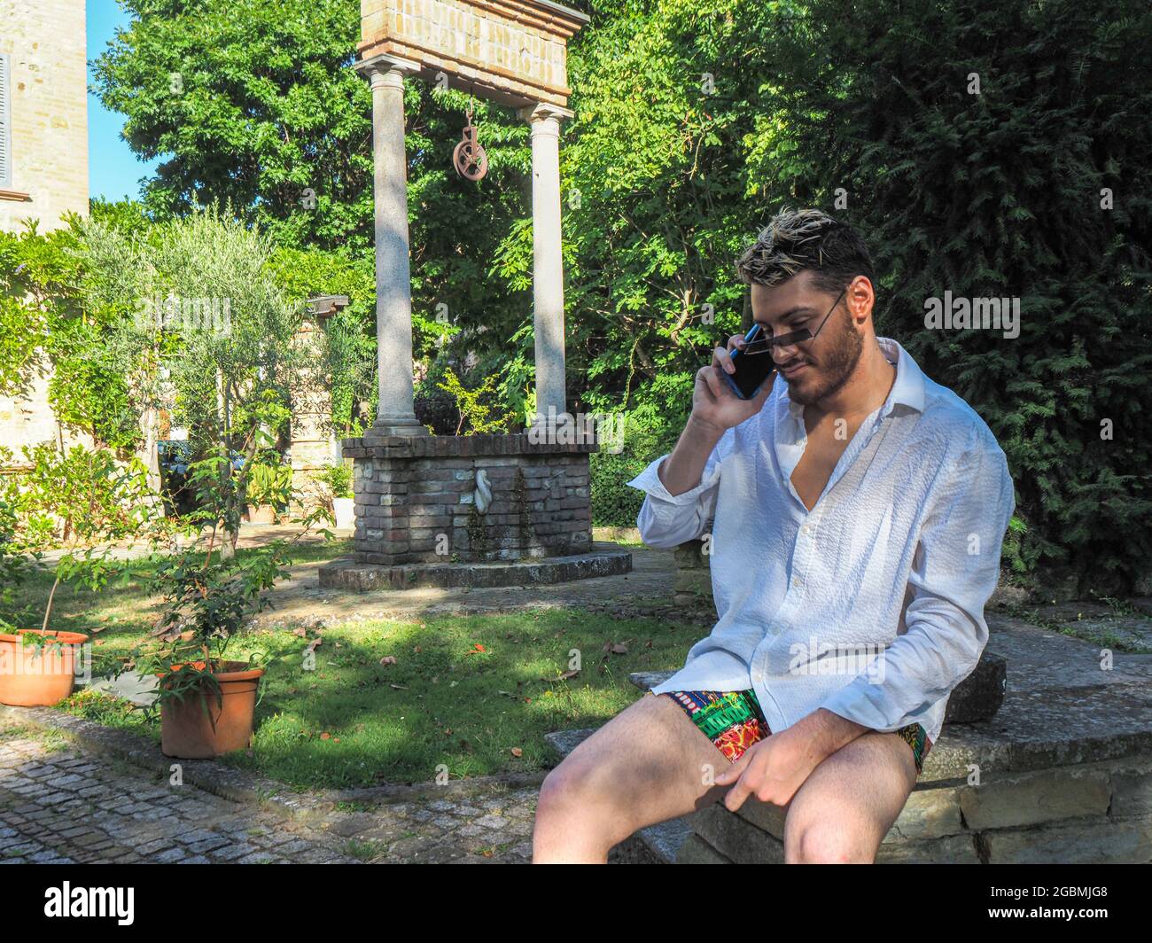 Gender-fluid Caucasian Italian person sitting in a garden, talking on ...