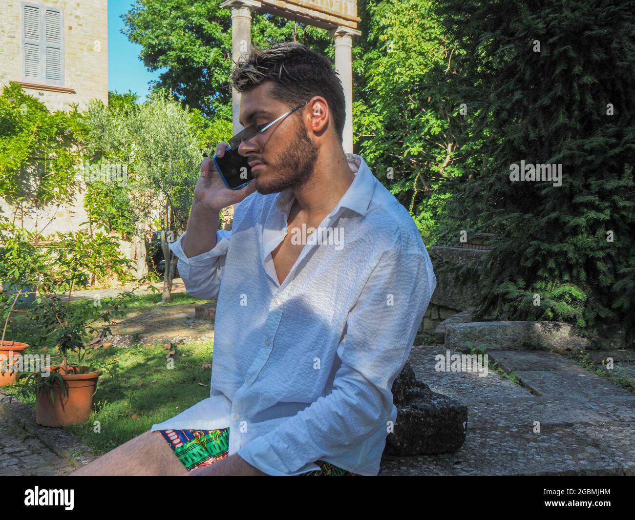 Gender-fluid Caucasian Italian person sitting in a garden, talking on ...