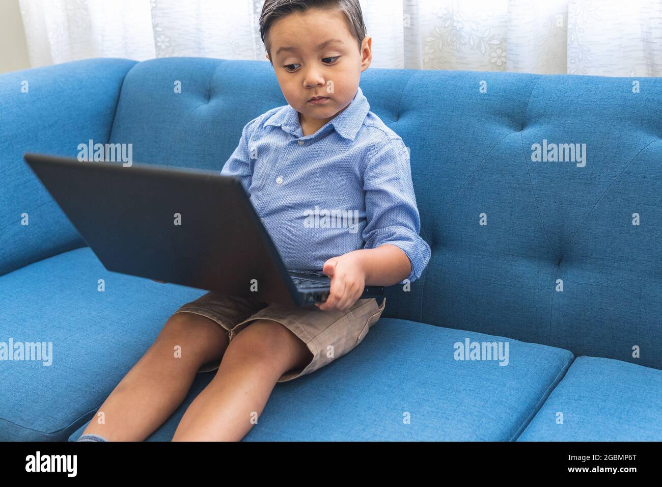 A pre-school child looks at a laptop monitor sitting on a sofa in his ...