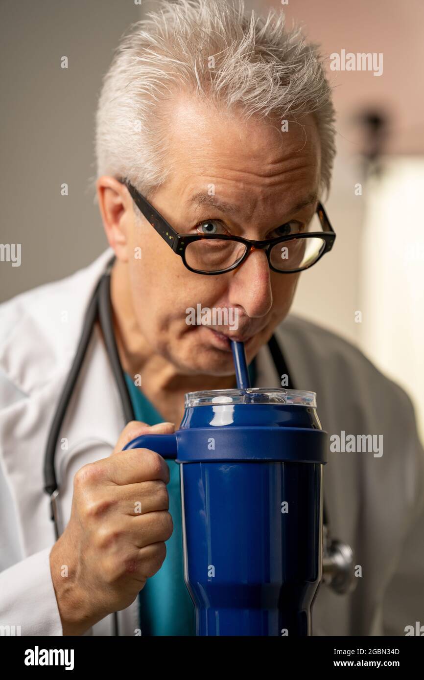 Handsome mature doctor drinking water from a cantine to keep hydrated ...