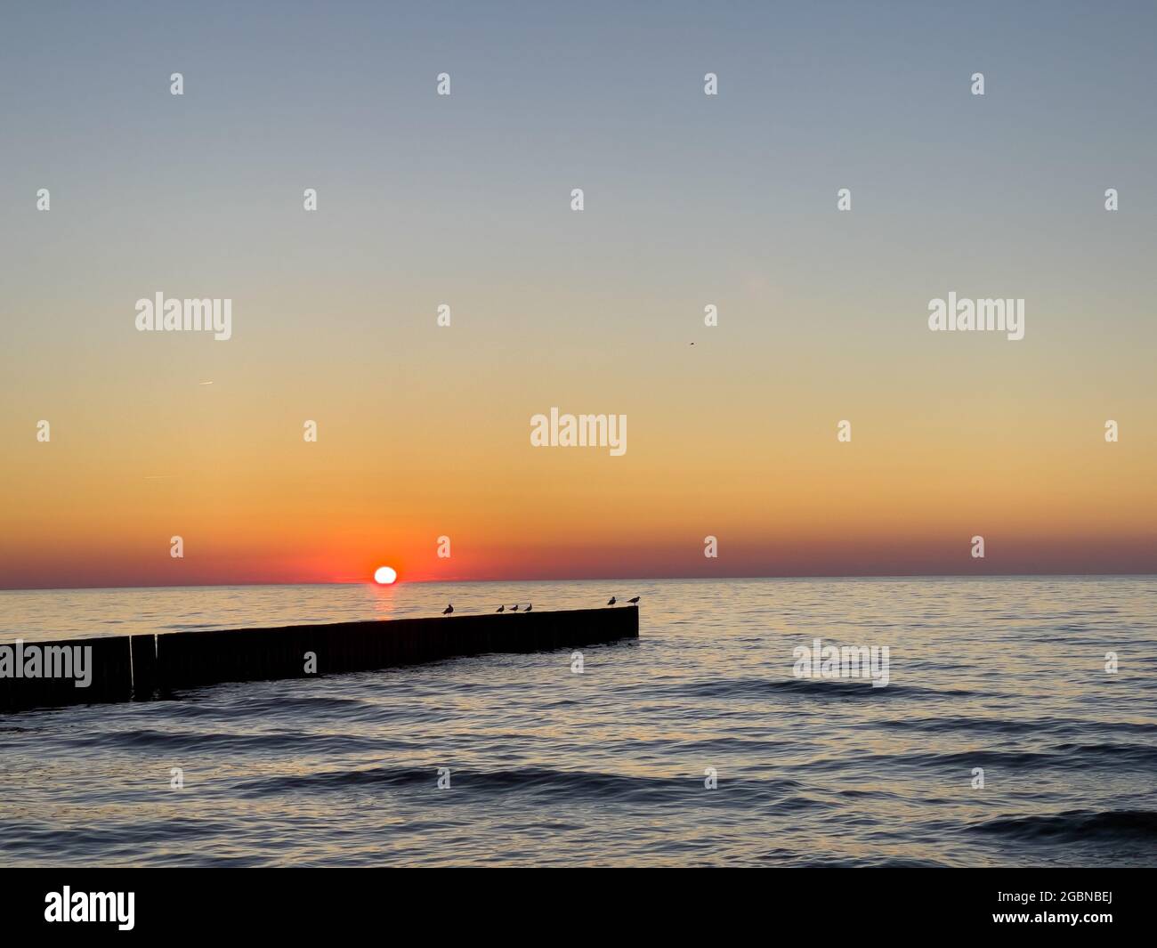 Red sun setting below the horizon in a gradient orange and blue sky at ...