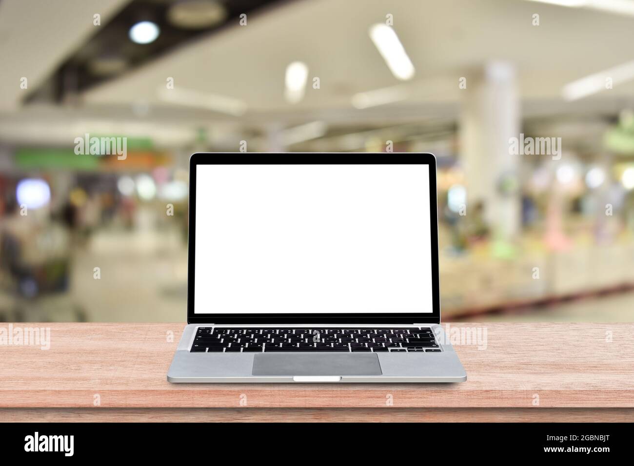 Laptop computer with blank screen on wood table over blur shopping mall ...